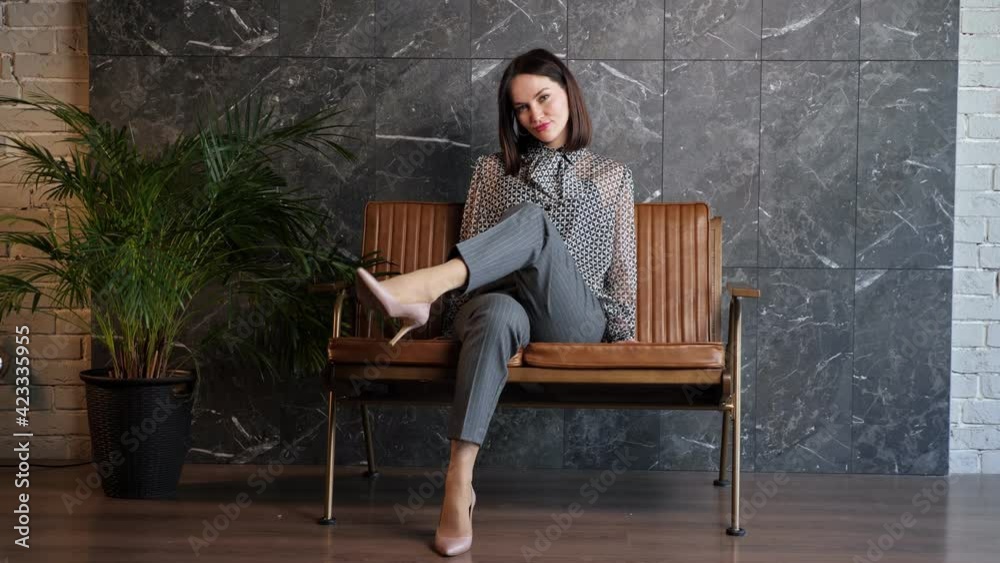Young brunette in grey classic costume sits on brown bench at marble ...
