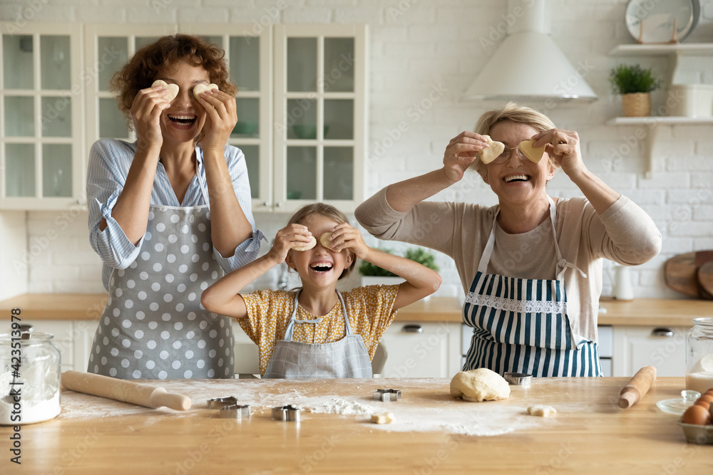 Smiling three generations of woman have fun baking sweet cookies ...