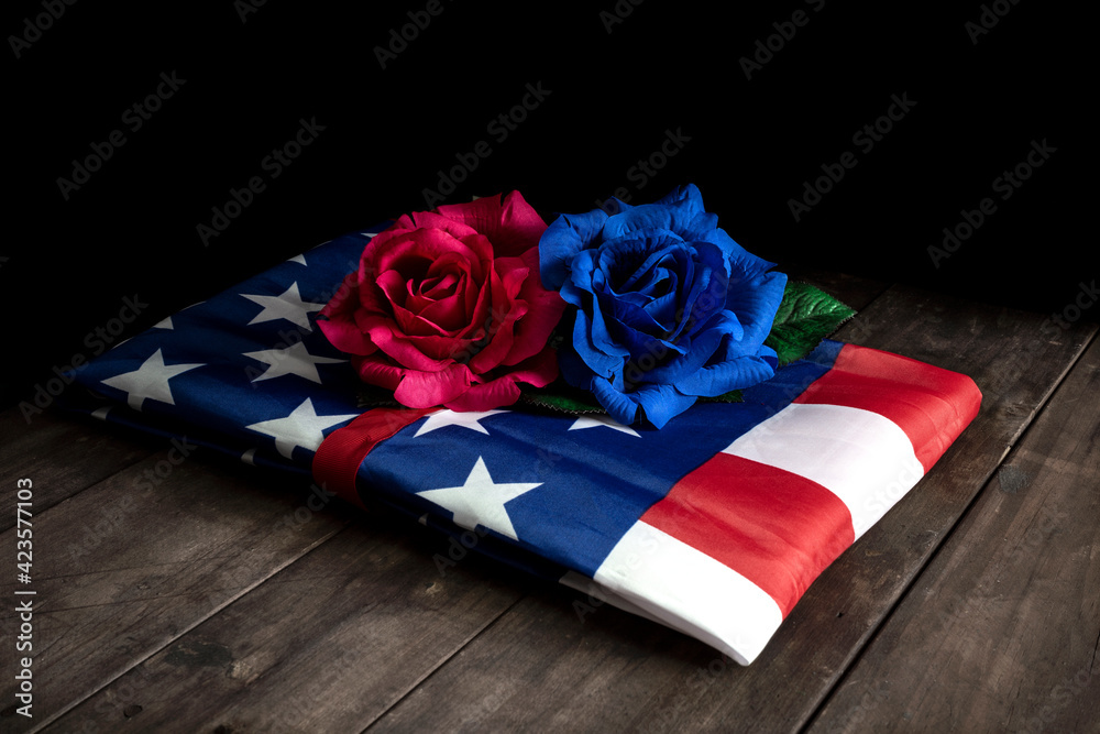 FOLDED FLAG OF THE UNITED STATES OF AMERICA WITH TWO ROSES, ONE RED AND ...