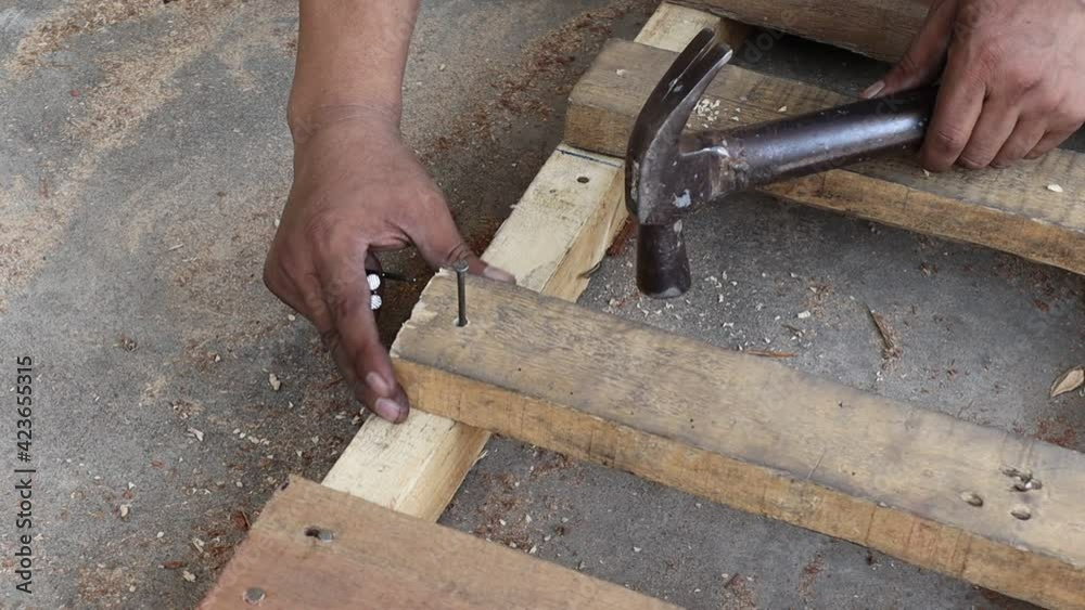 Man used metal hammer is hitting the nails on wooden bar for making ...