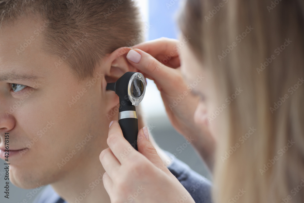 Doctor holding otoscope in his hand in front of patient ear closeup ...