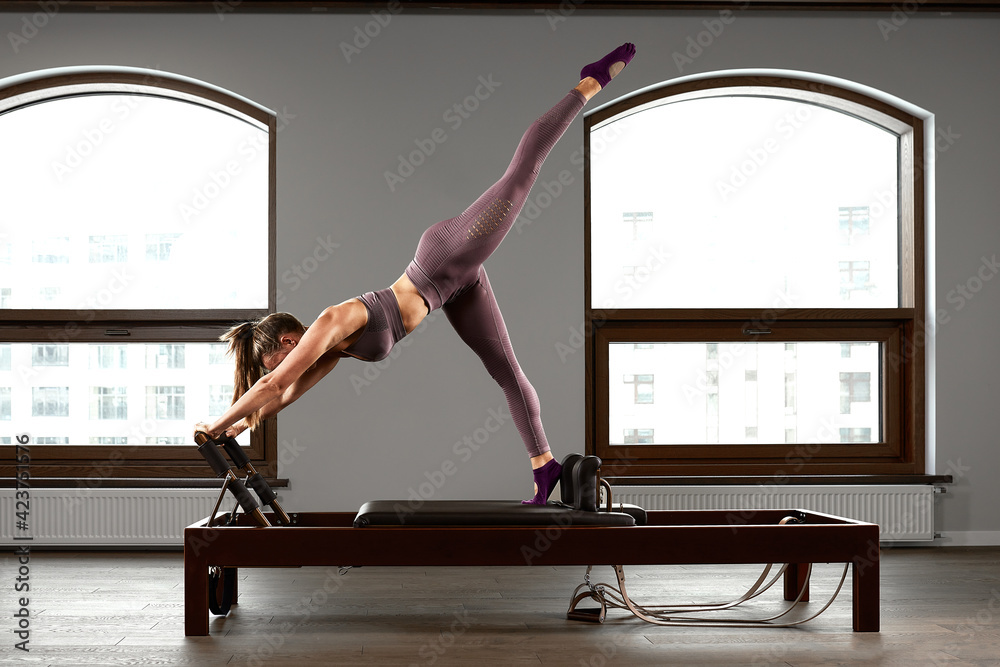 Young girl doing pilates exercises with a reformer bed. Beautiful slim ...
