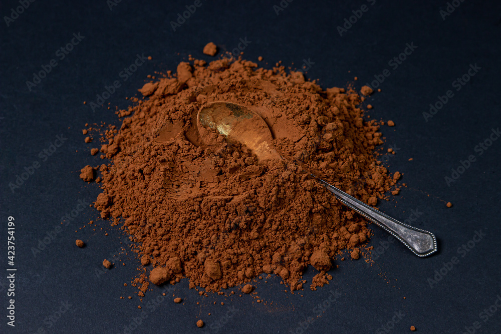 Cocoa powder on a black background. The spoon lies in cocoa powder on a ...