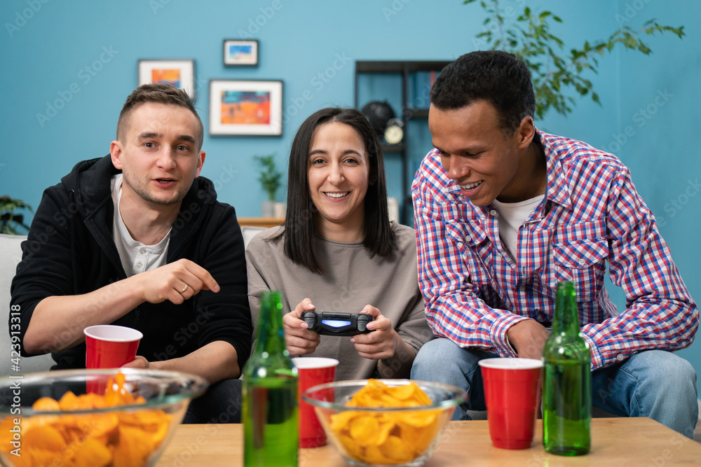 Multinational friends sitting at home on couch and playing video games ...