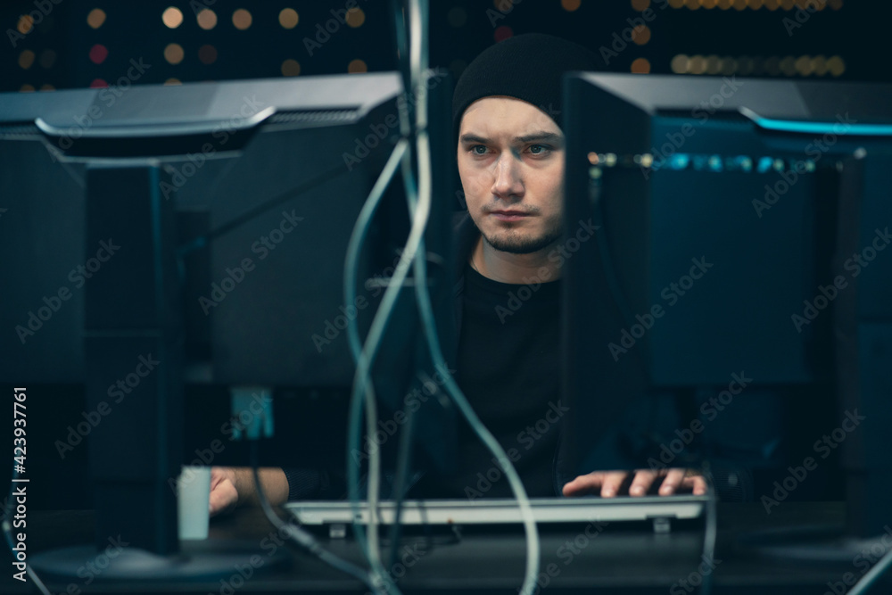 Young professional male hacker using keyboard typing bad data into computer online system and ...