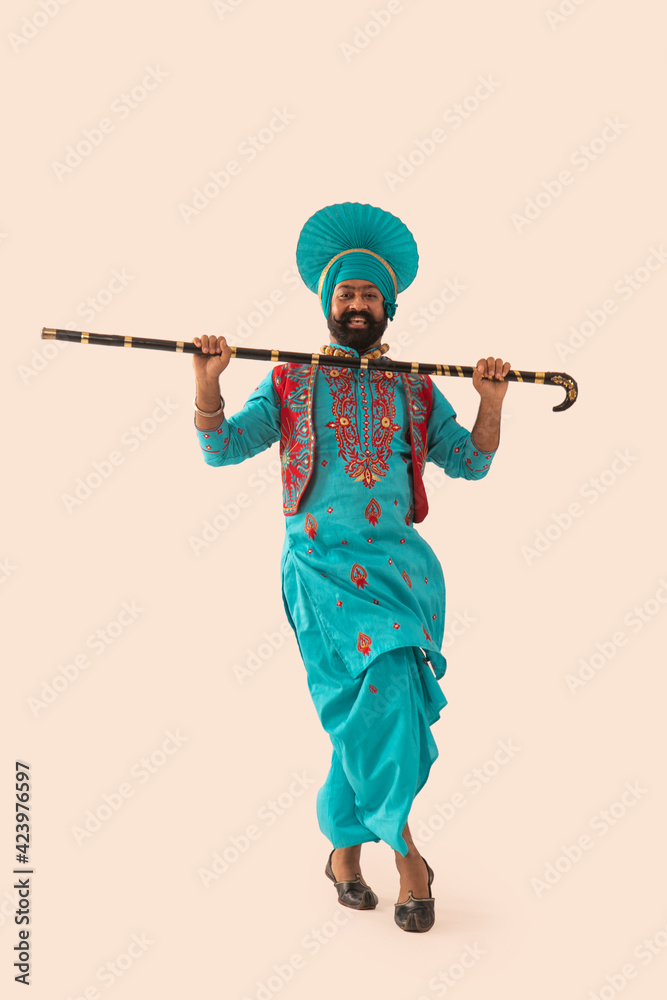 A Bhangra Dancer standing cross- legged holding a Khunda happily. Stock ...