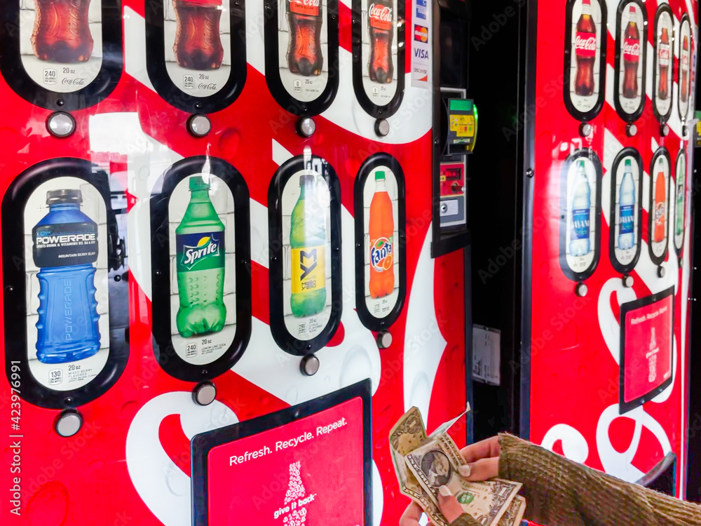 Hands holding money in front of Coca-Cola soda vending machine on March ...