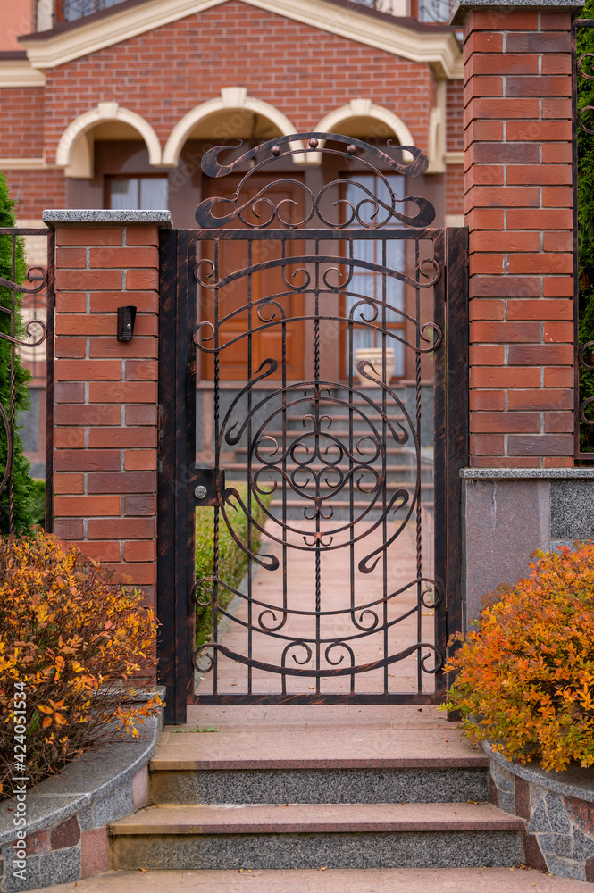 forged metal gate with brick pillars in front of the house on the ...