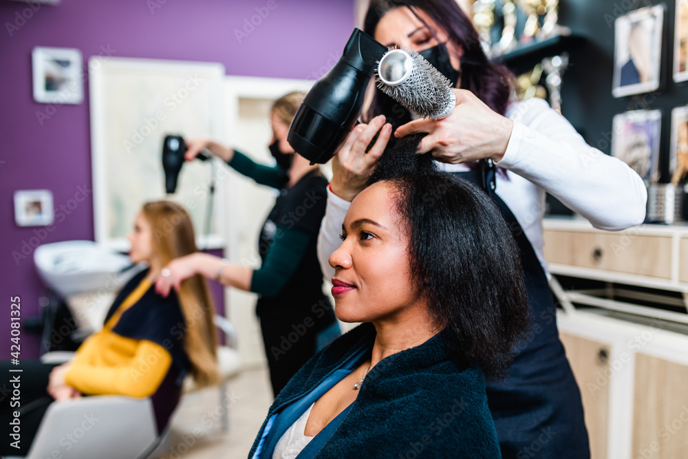 A hairdresser dries a Black woman's hair in a modern hair salon. Beauty ...