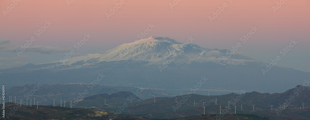 Etna volcano in the sunset. Many wind turbines can be seen in the ...