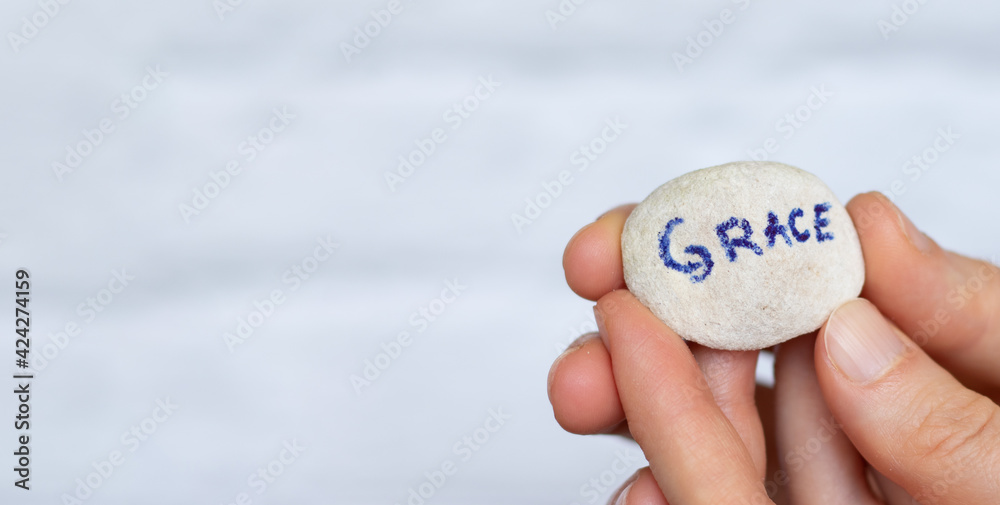 Woman's hand holding stone with handwritten word grace against white ...