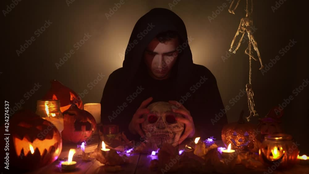 An evil man in a gothic dark cloak is sitting and touching the ritual ...