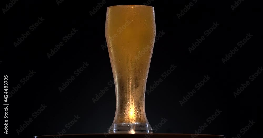 Cold beer in glass rotate in surface with black background. Detail Shot ...