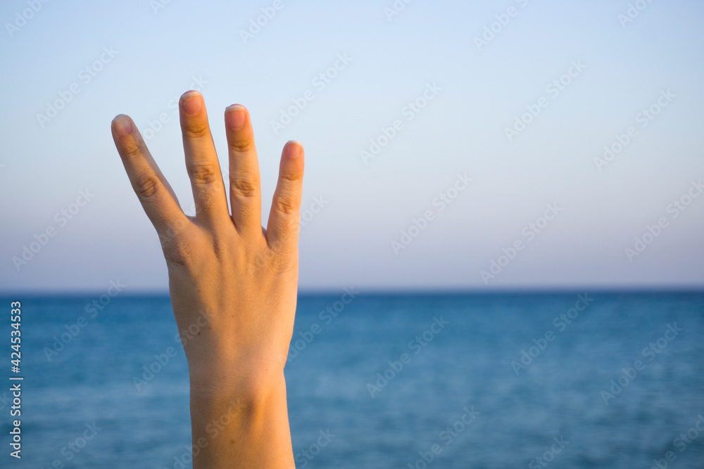 Hand doing showing number four gesture symbol on blue summer sky nature ...