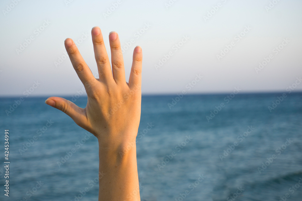 Woman hand doing showing number five gesture symbol on blue summer sky ...