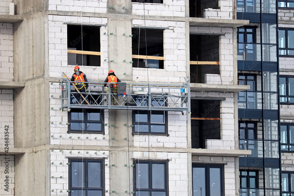 Workers standing on lifting platform near the wall of unfinished house ...