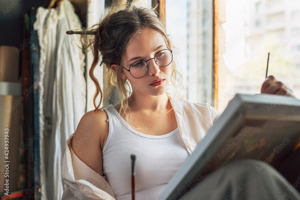 Female artist painting on canvas in her art studio sitting next to the ...