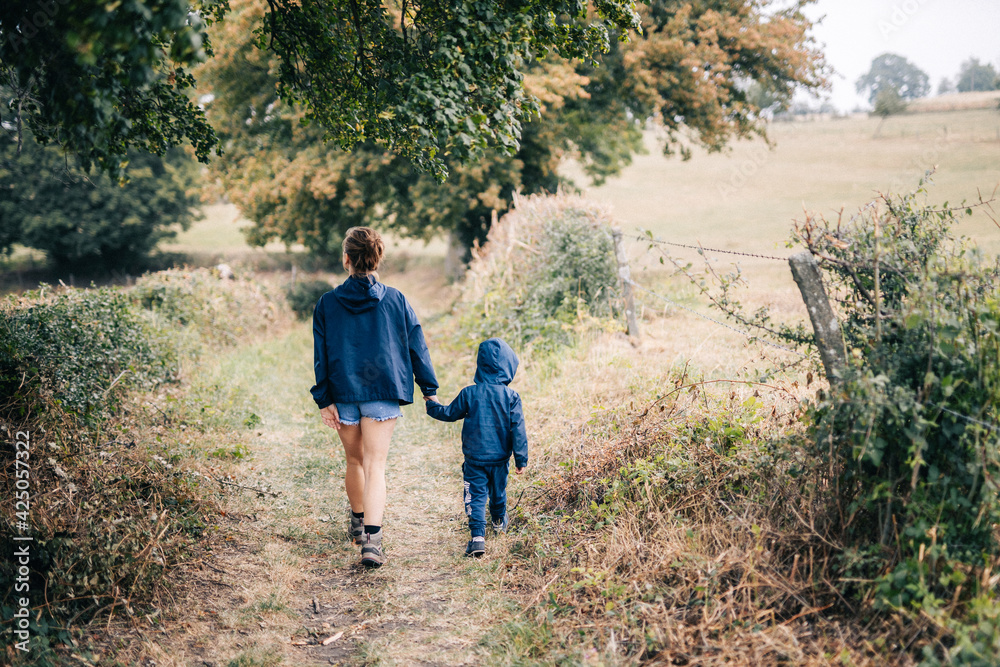 Maman se balade avec son enfant, main dans la main, de dos, en été sous ...