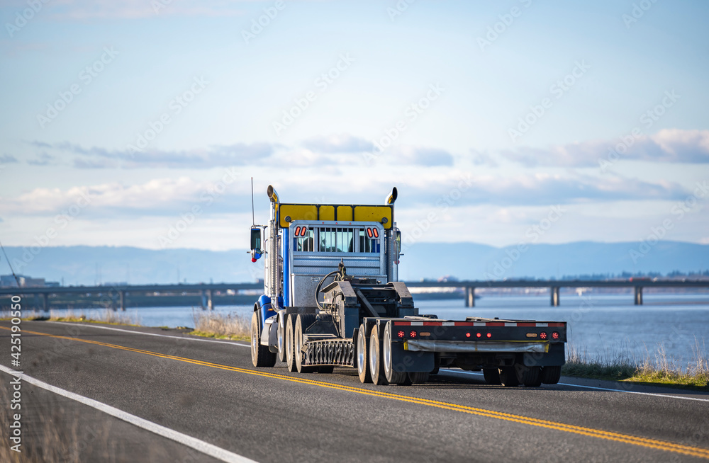 Big rig blue day cab semi truck transporting empty step down semi ...