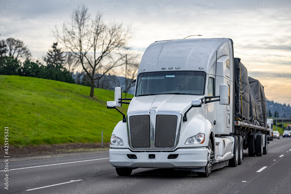 Huge white big rig semi truck tractor transporting covered cargo on ...