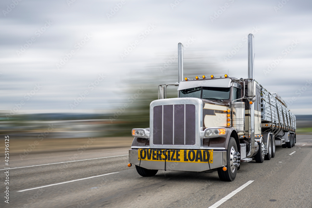 Powerful classic dark big rig semi truck with oversize load sign on the ...