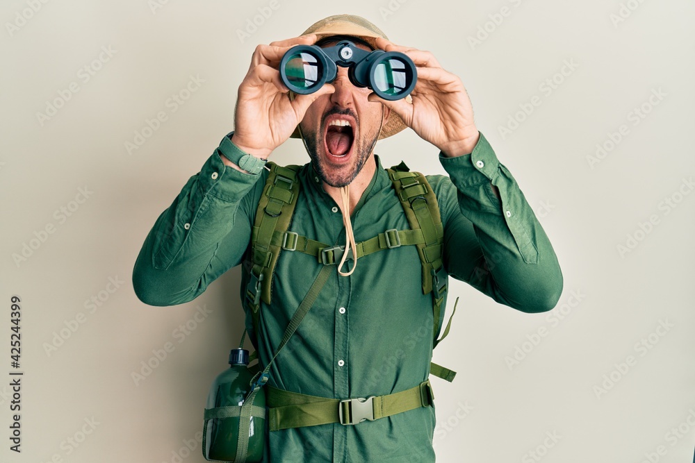 Handsome man with beard wearing explorer hat looking through binoculars ...