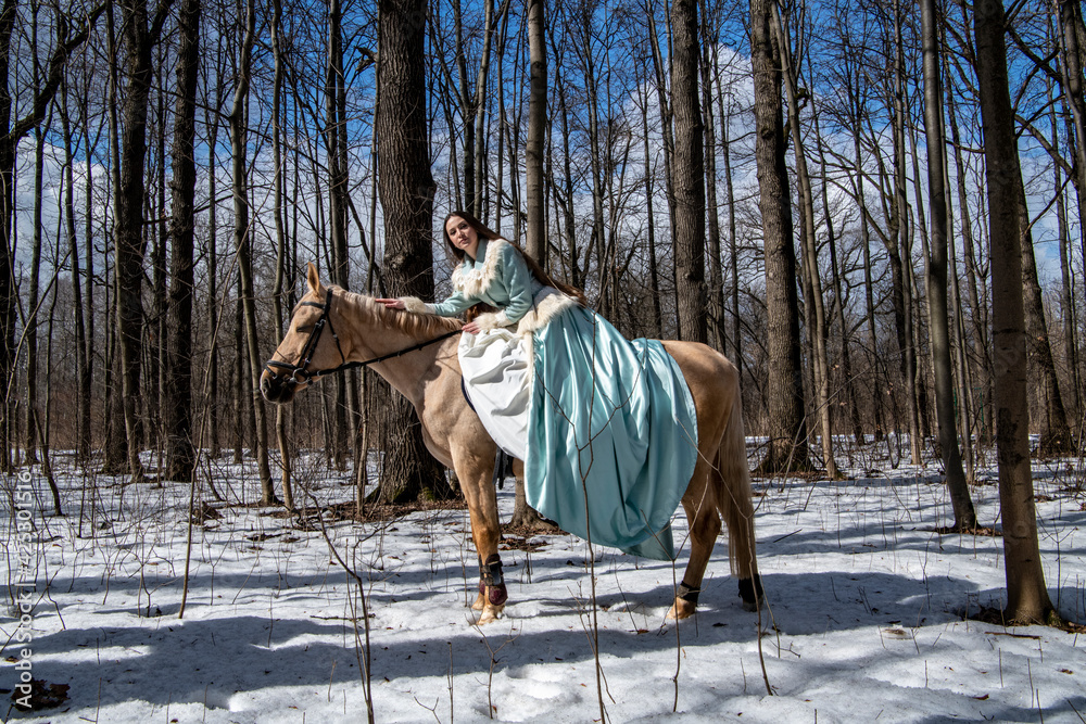 beautiful girl in a blue outfit and a light brown horse in a spring ...