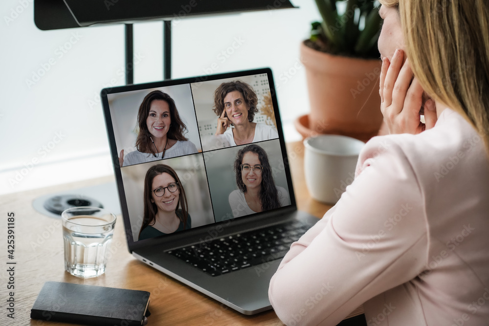 back of a remote online coaching woman sitting on her work desk infront ...
