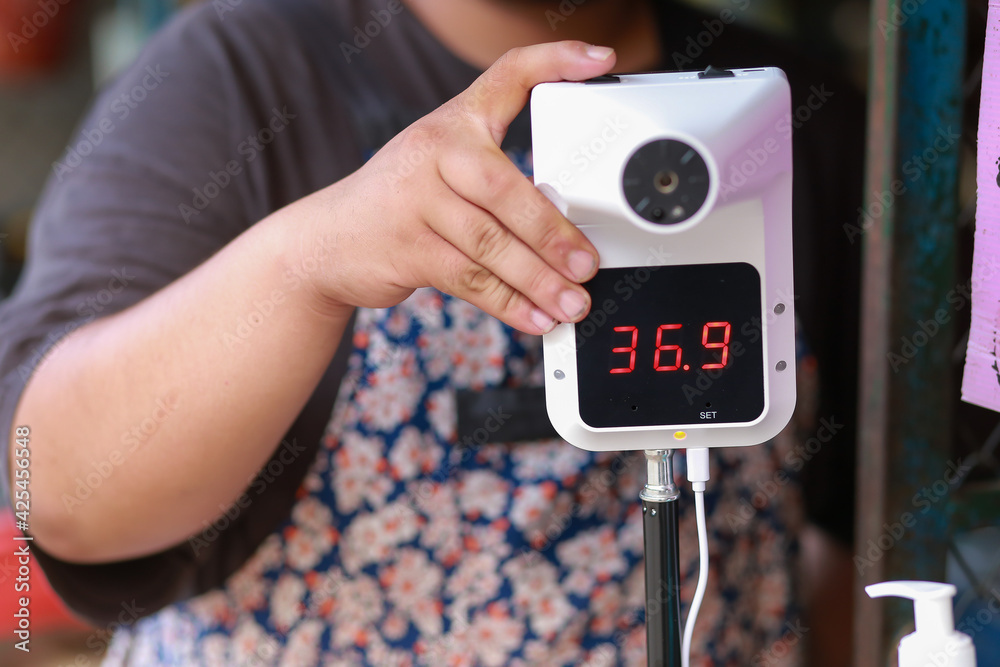 A fever meter with a stand and a man's hand is measuring fever in ...