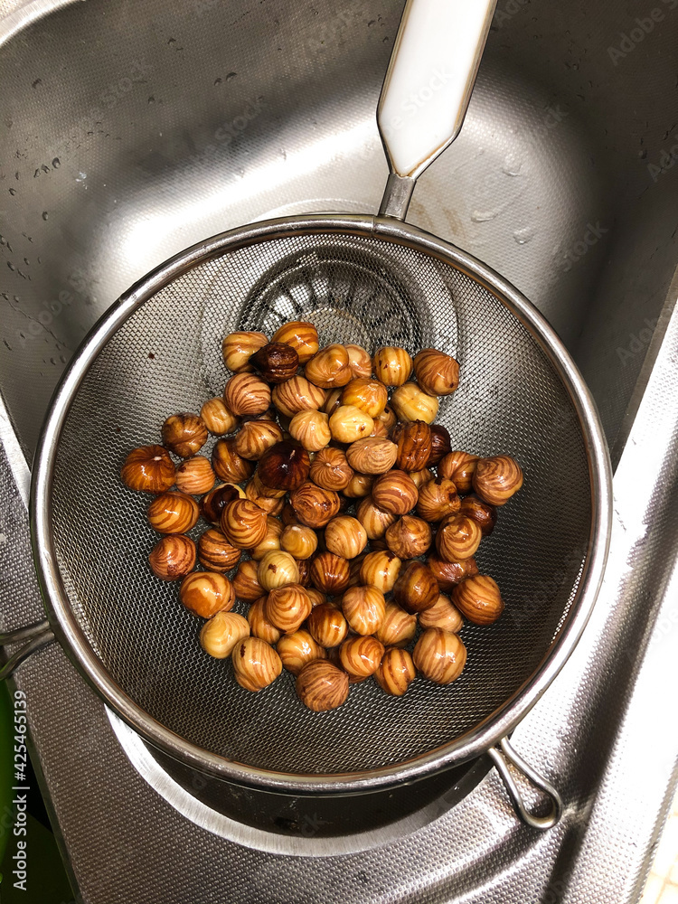 A handful of washed hazelnuts lies in a colander in a metal sink ...