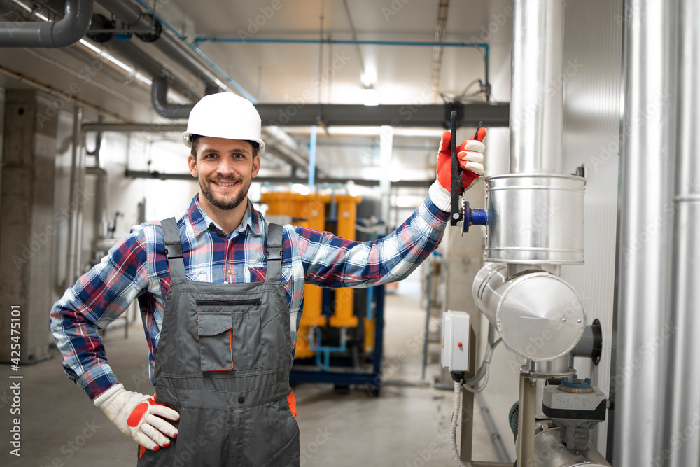 Portrait of factory engineer worker holding his arm on the valve and ...