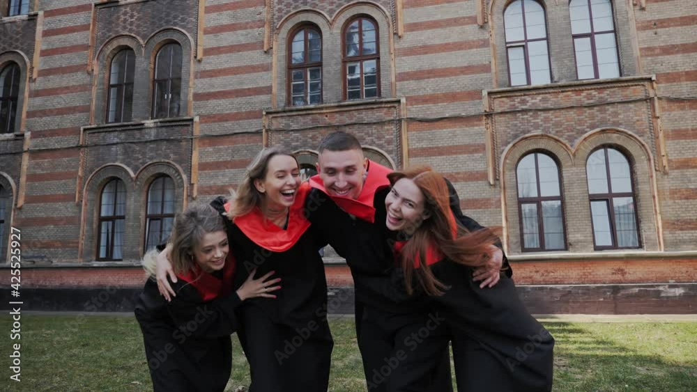 Female and male college graduates in graduation gowns laughing hugging ...