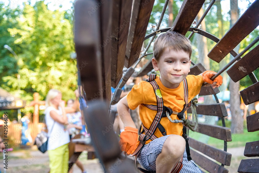 Happy kid overcomes obstacles in rope adventure park. Summer holidays ...