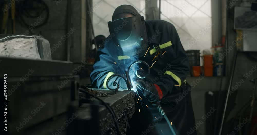 Welder welds metal details in safety uniform at his workroom, welding ...