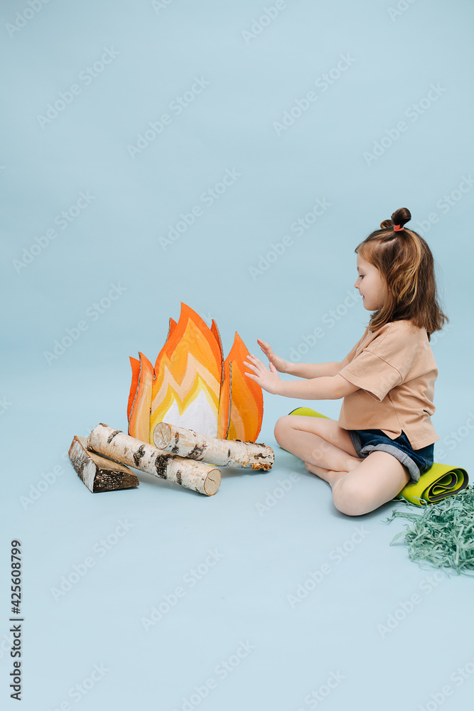 Subtly smiling little girl sitting next to fake campfire, pretending to ...