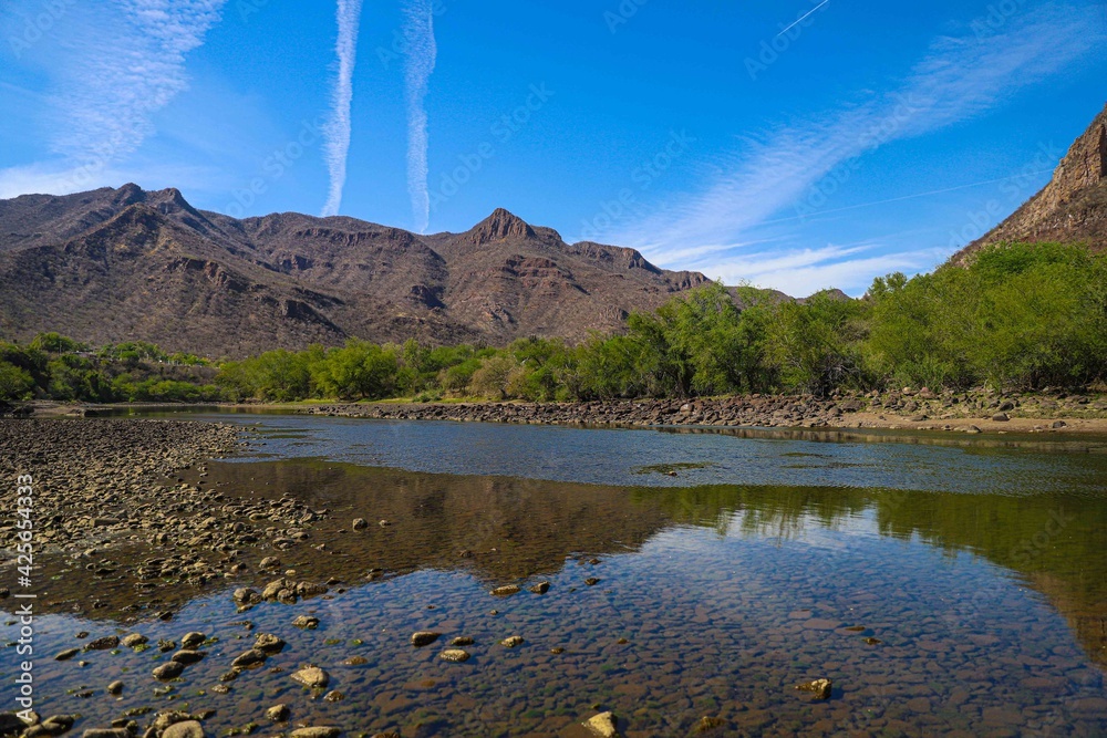 Reflection of a hill and bushes in the water of the Yaqui River as it ...