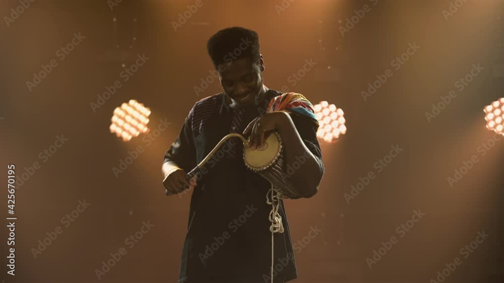 Black musician plays talking African yuka drum in a dark studio against ...