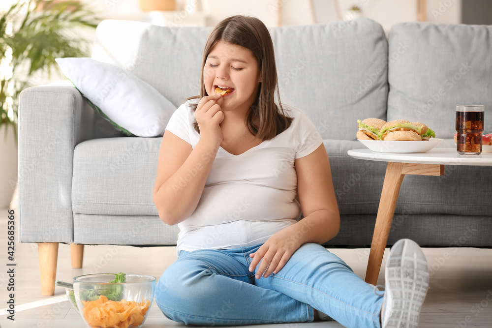 Overweight girl eating unhealthy chips at home Stock Photo | Adobe Stock