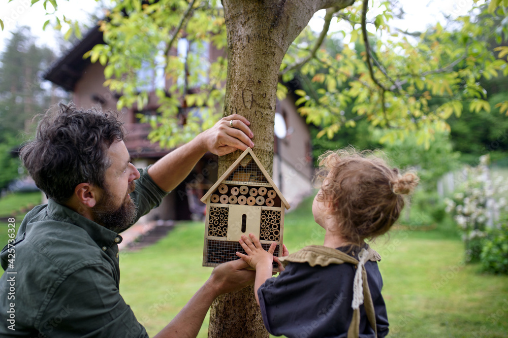Small girl with father holding bug and insect hotel in garden ...
