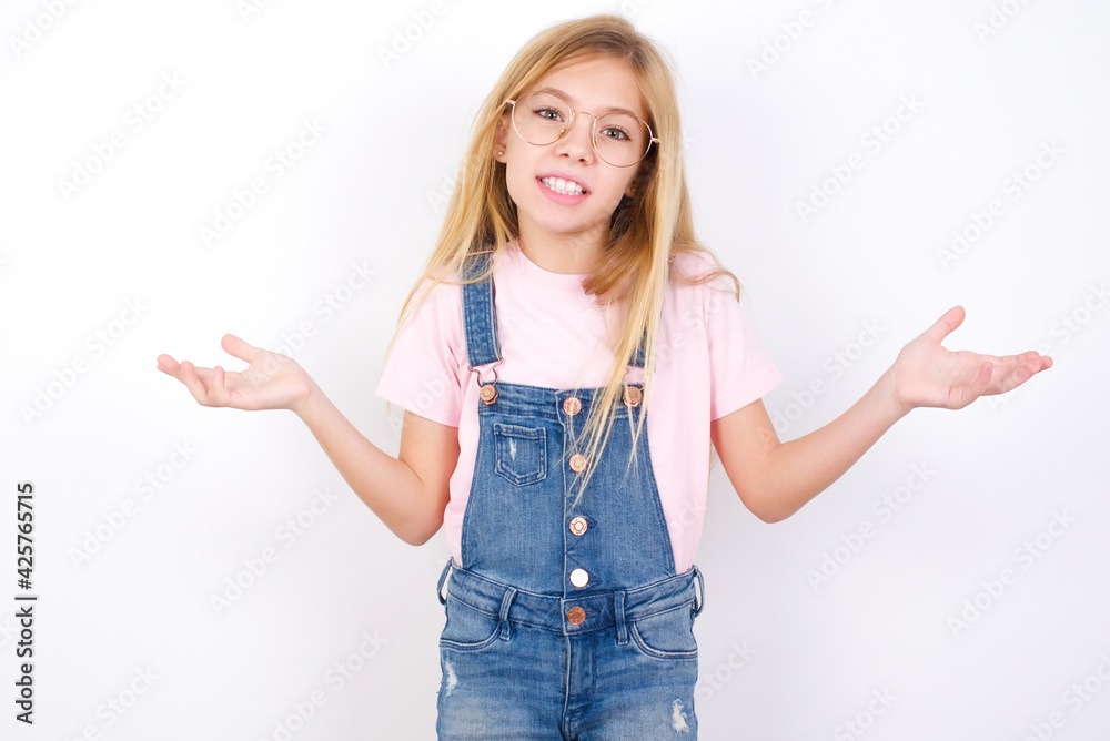 Clueless beautiful caucasian little girl wearing jeans overall over ...