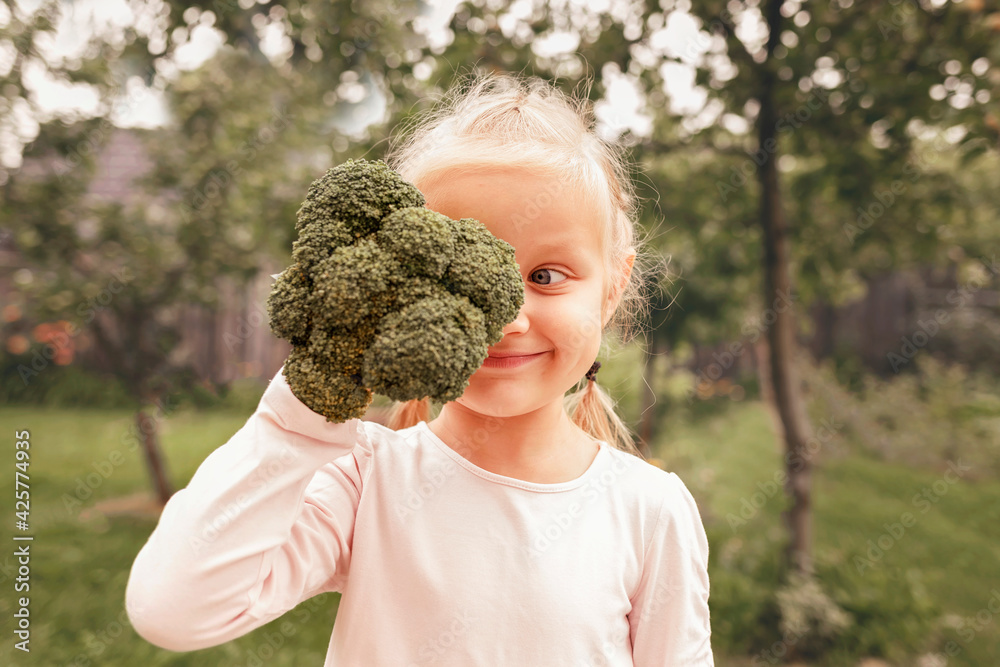 Little girl holding green broccoli in front of her face. Green broccoli ...