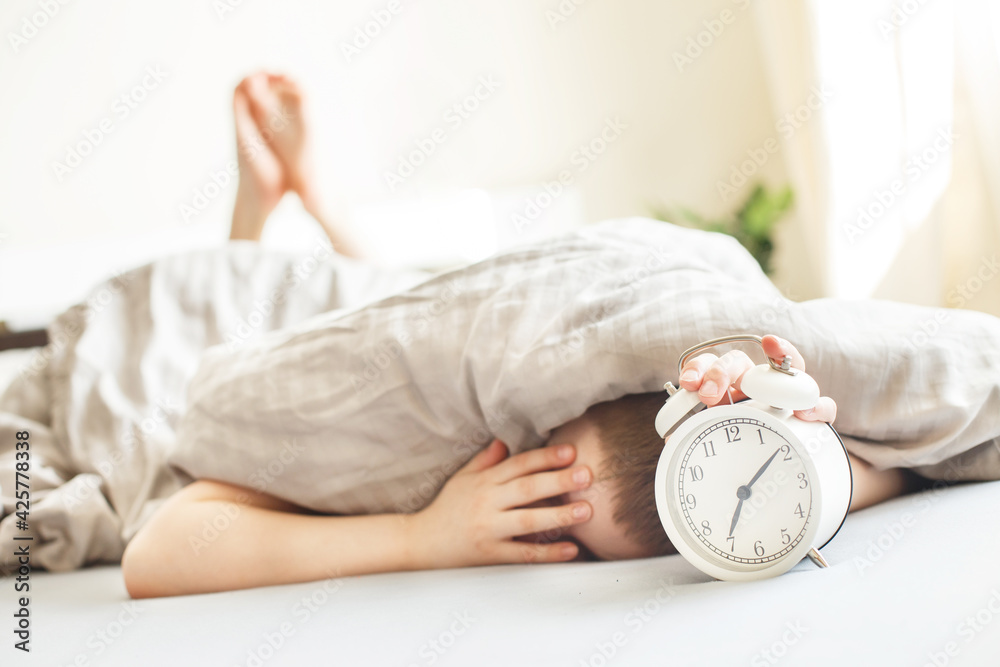 boy lying on the bed and stopping alarm clock in morning. childs hand ...