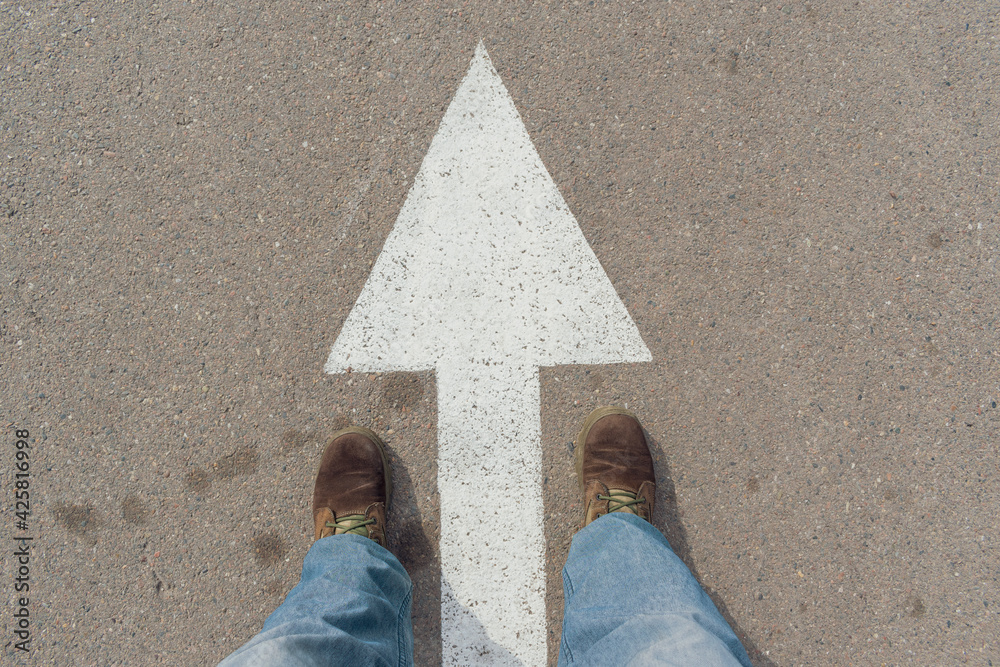 Male feet in boots and jeans. The white arrow on the pavement shows the ...
