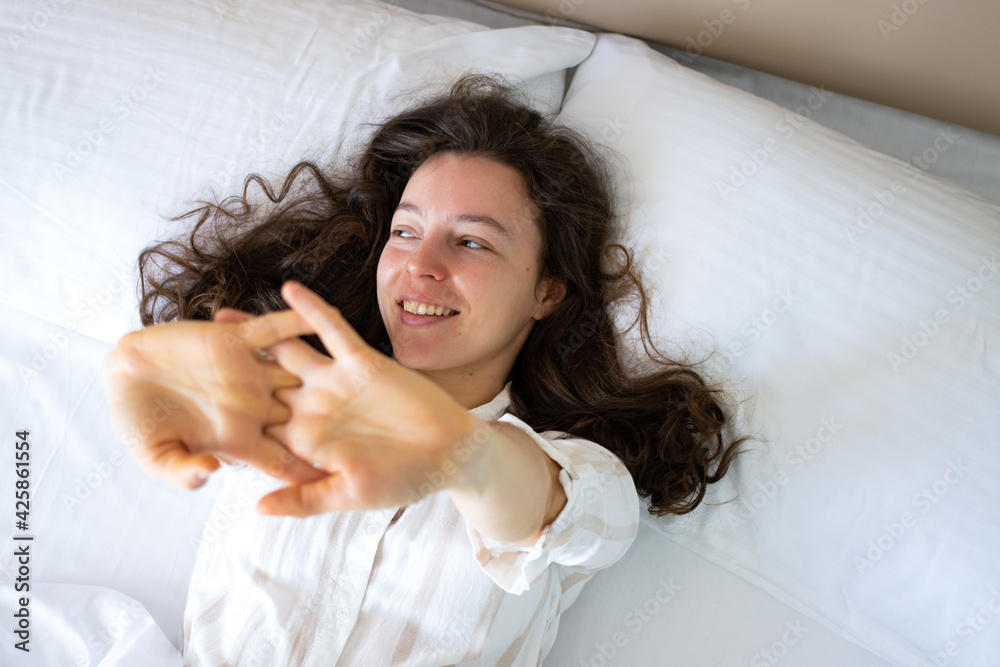 Beautiful happy young woman waking up, stretching arms raising hands up ...
