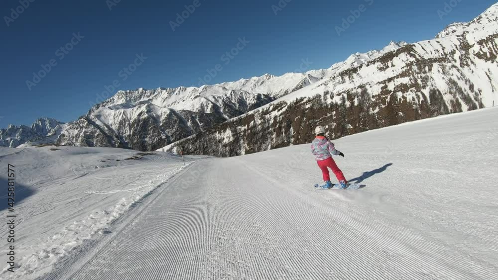 A snowboarding woman in pink outfit going down a perfectly groomed ...