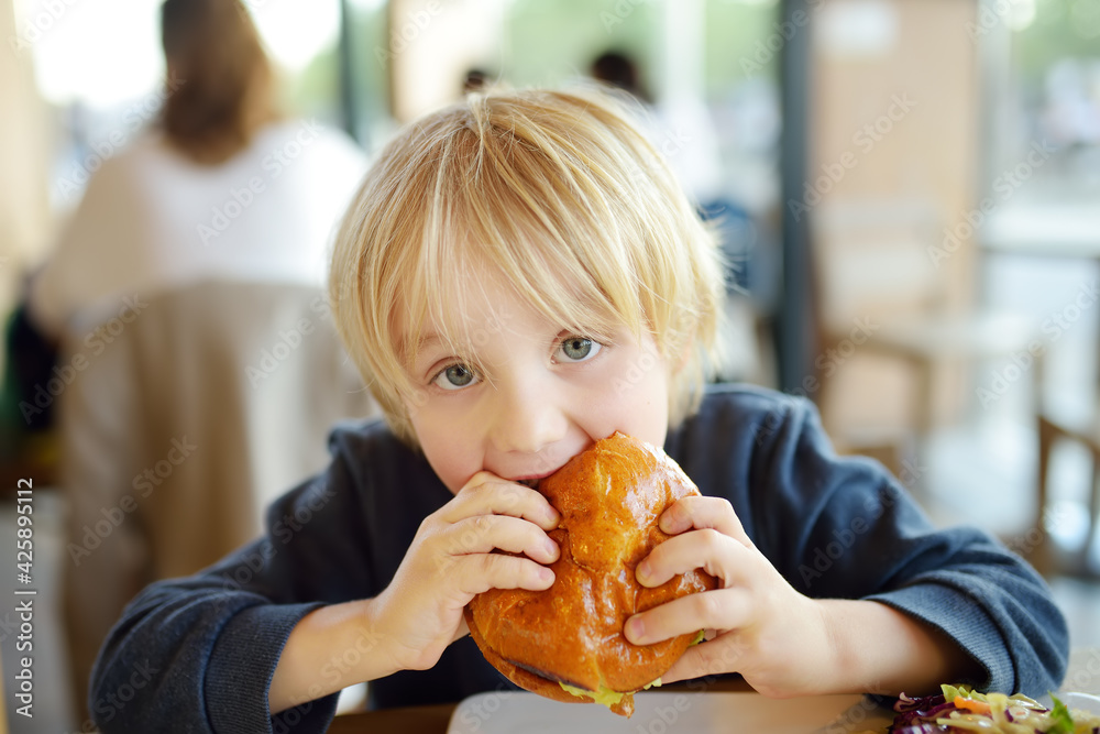 Cute preschooler boy eating large hamburger at fast food restaurant ...