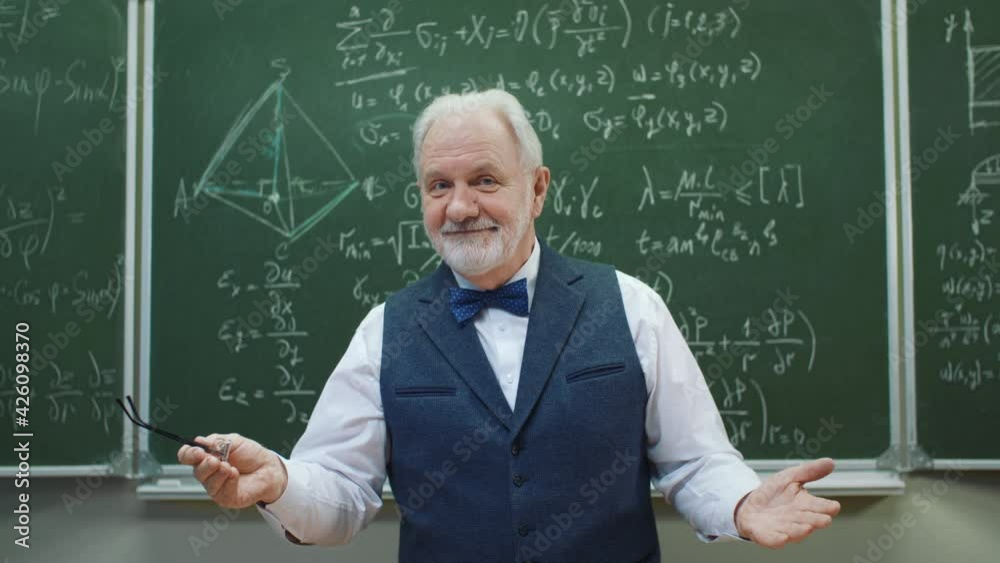 Intelligent senior teacher in university classroom standing looking at ...