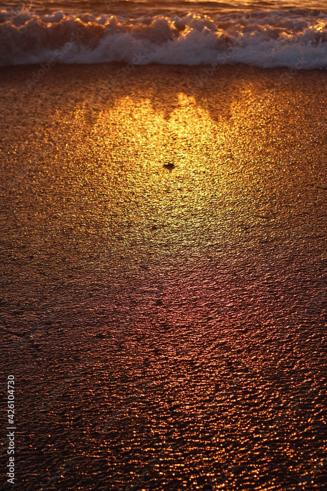 Gold and rainbow water on the sand at the beach. Retreating ocean wave ...