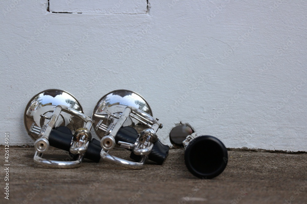 Two silver trumpets and a black wooden clarinet placed on the ground ...
