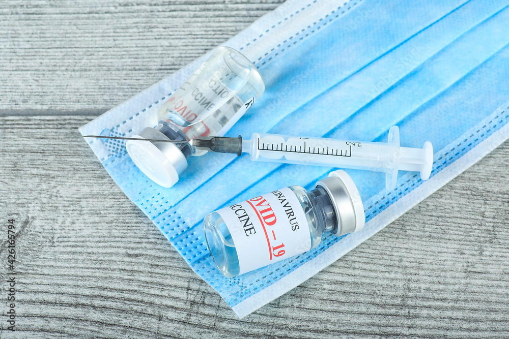 Coronavirus vaccine, syringe and medical face mask on the wooden desk ...